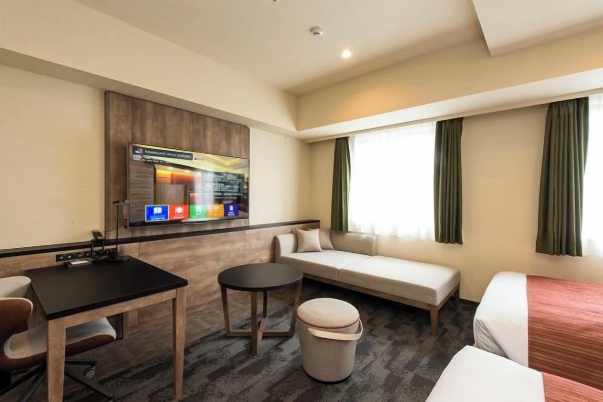 Quarto de hotel com sofá, cama, escrivaninha e lixeira.