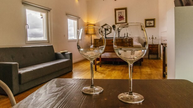Um quarto com uma mesa de madeira, dois copos de vinho, um sofá cinzento e um lustre.
