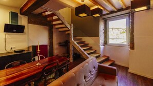 Uma sala de jantar com uma mesa e cadeiras de madeira, um banco estofado, uma escada e uma janela com vista.