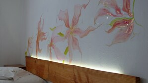 Quarto com cabeceira de madeira, cama com roupa de cama branca e parede com pintura floral.