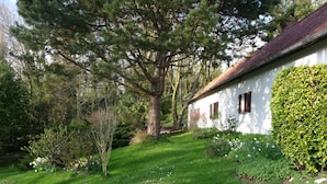 Um edifício branco com telhado inclinado, rodeado por um jardim bem cuidado com diversas plantas e flores.