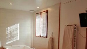 Casa de banho moderna com banheira, duas cadeiras pretas, um tapete vermelho e uma janela com persianas.