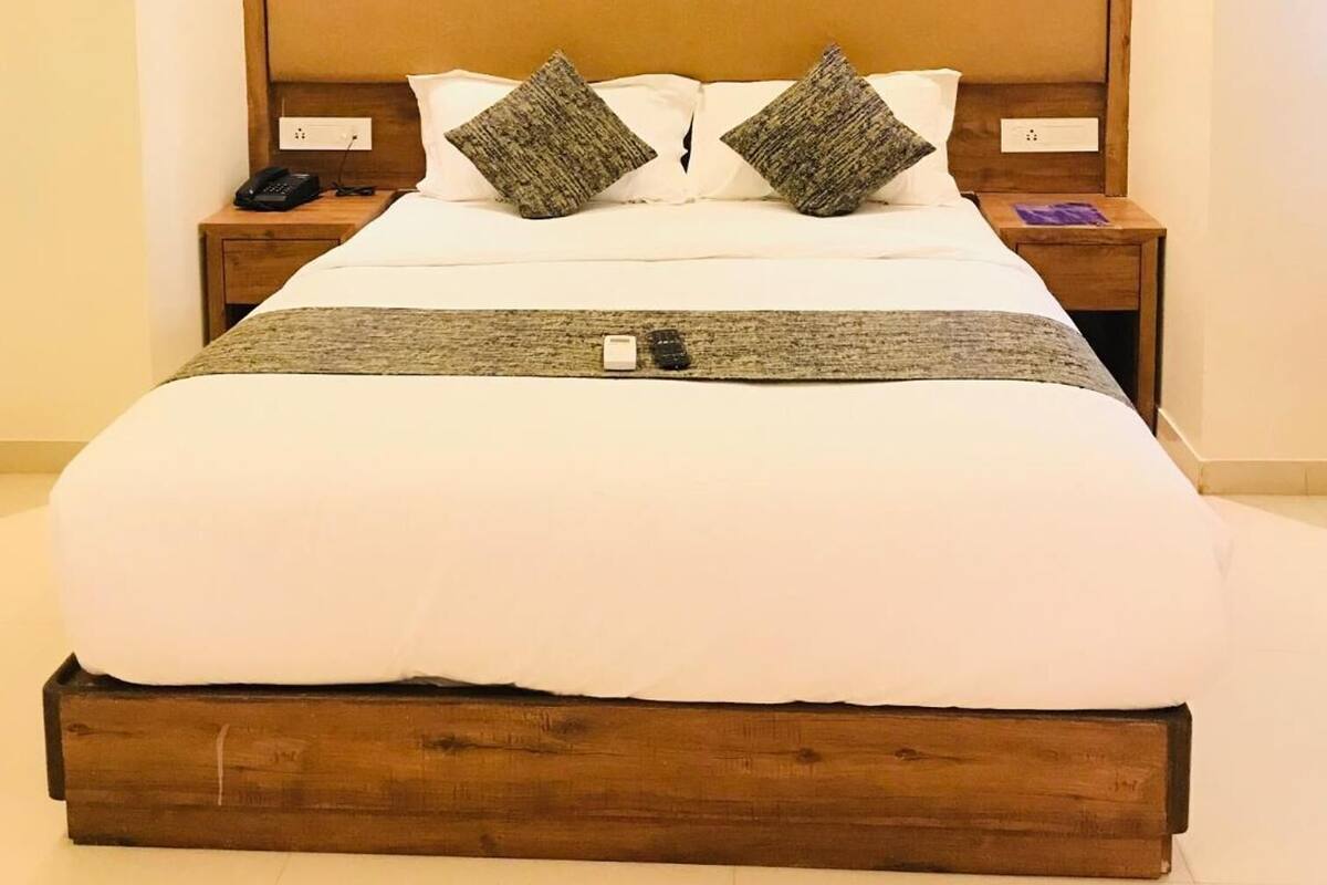 Quarto de hotel com cabeceira de madeira, duas almofadas, mesa de cabeceira com telefone e um cobertor na cama.
