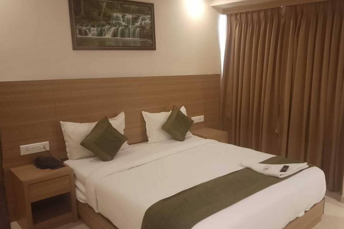 Quarto de hotel com uma cama grande, uma mesa de cabeceira, um quadro na parede e uma janela com cortinas.