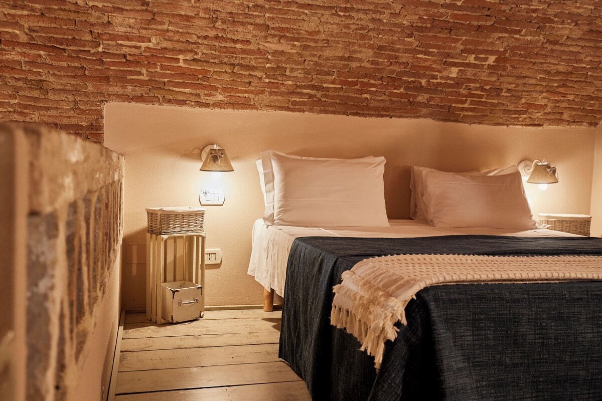 Um quarto aconchegante com teto de tijolos, piso de madeira, cama com roupa de cama branca e duas luminárias de cabeceira.