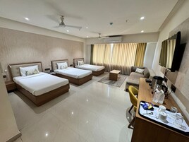 Quarto de hotel com três camas, um sofá, um espaço para café e uma televisão na parede.