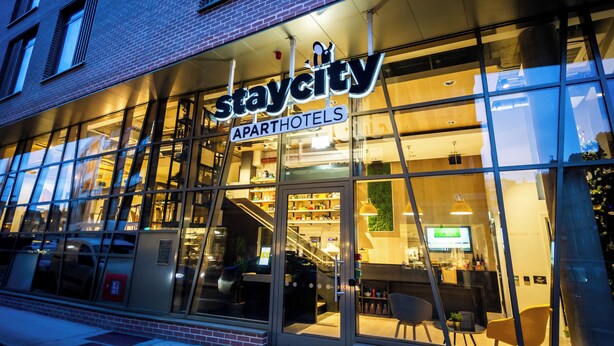 Um hotel-apartamento Staycity com grandes janelas, uma escadaria visível e uma área de recepção.