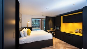 Quarto de hotel moderno com uma cama grande, uma kitchenette pequena e vista para a cidade pela janela.