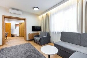 Uma sala de estar moderna com um sofá cinza, uma mesinha branca e uma televisão de tela plana.