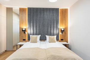 Quarto de hotel moderno com uma cama grande, duas mesas de cabeceira e cabeceira com linhas verticais.