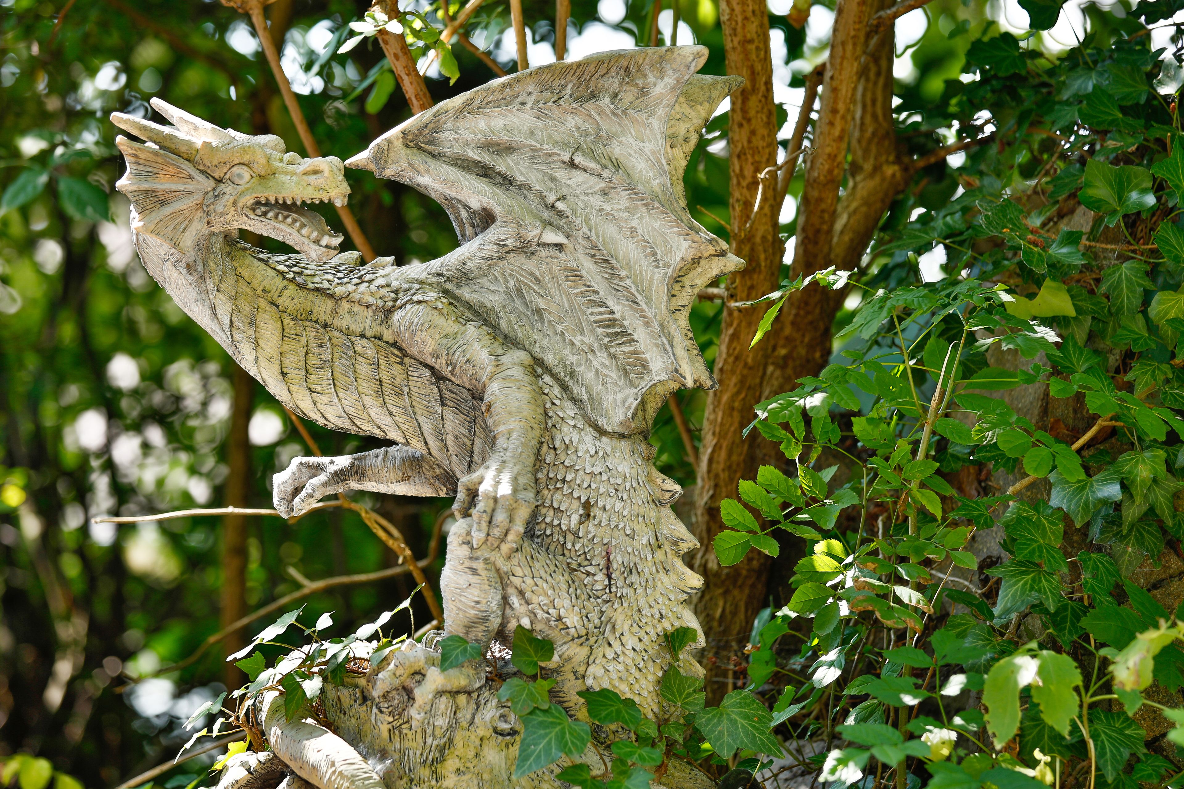 Escultura de dragão de pedra cercada por vegetação.