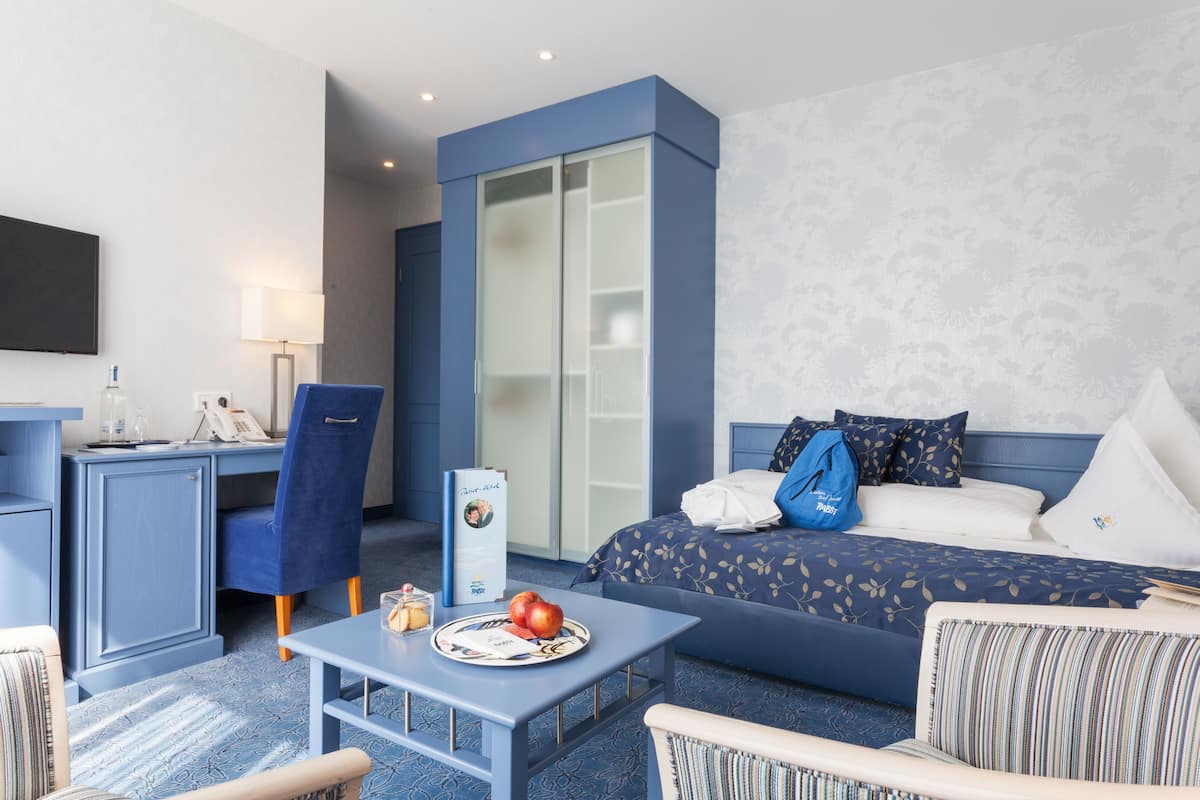 Quarto de hotel com cama, escrivaninha, cadeira, mesa com uma travessa de fruta e televisão.