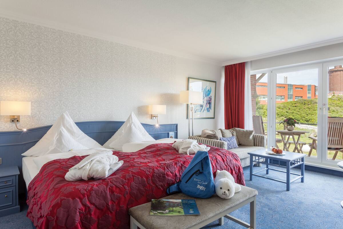 Quarto de hotel com uma cama grande, um banco, uma mesa pequena e vista para o exterior.
