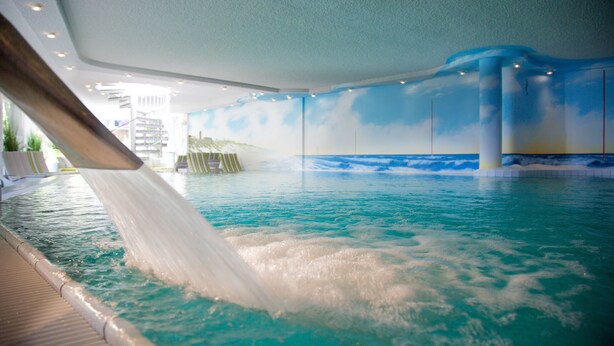 Piscina interna com efeito de ondas, um mural no teto e vista para o exterior.