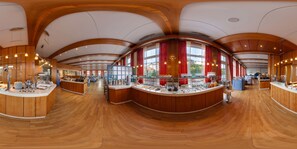 Uma área de buffet espaçosa e sinuosa, com piso de madeira e teto alto, com um balcão de serviço central e várias áreas de estar.