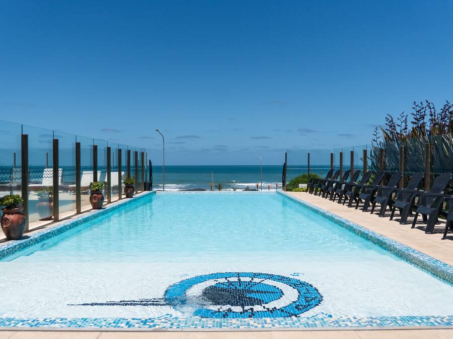Piscina com vista para o oceano, rodeada por espreguiçadeiras e plantas em vasos.