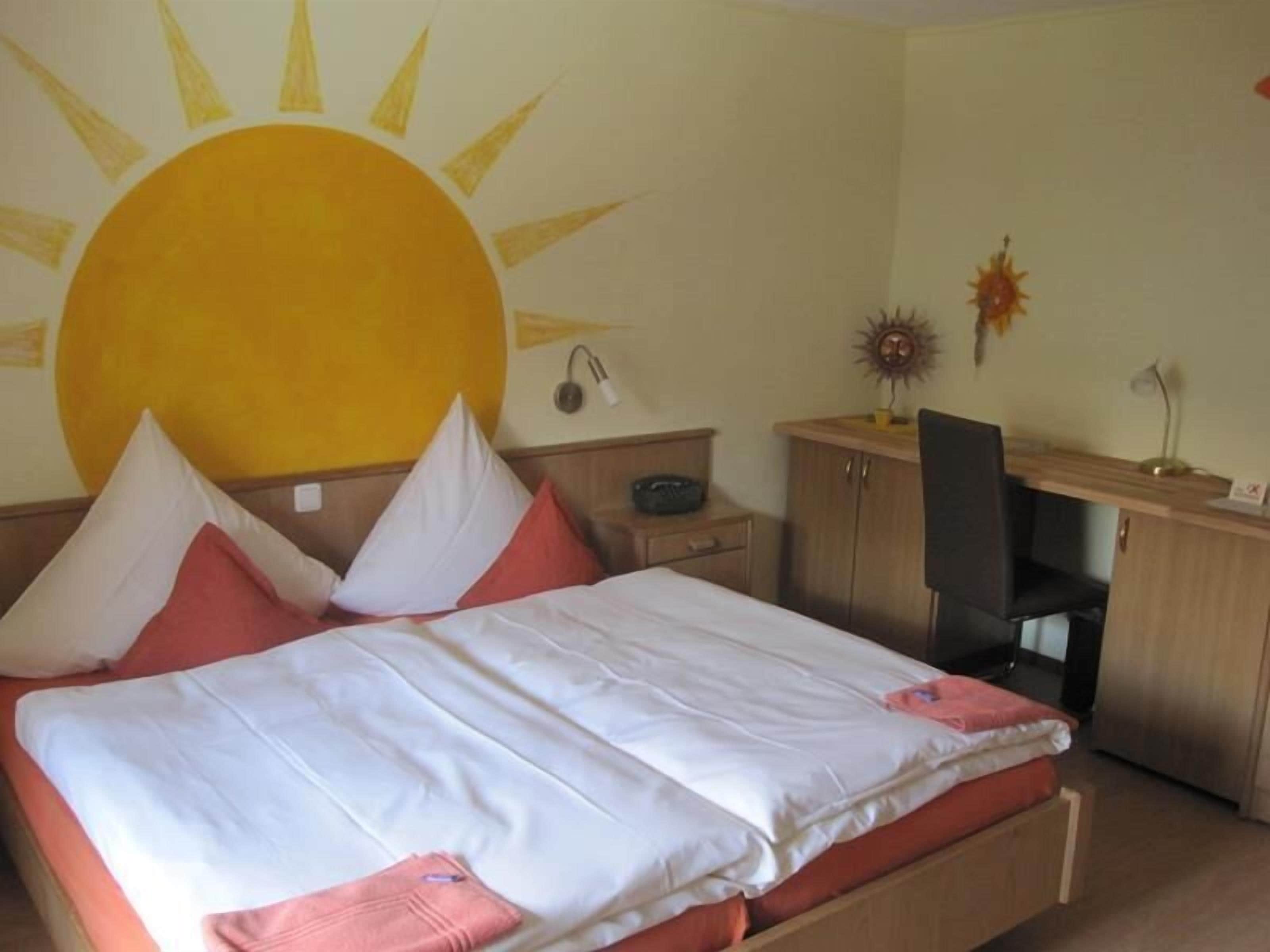 Um quarto com cama, almofadas, escrivaninha e um objeto decorativo na parede.