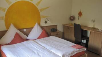 Um quarto com cama, almofadas, escrivaninha e um objeto decorativo na parede.