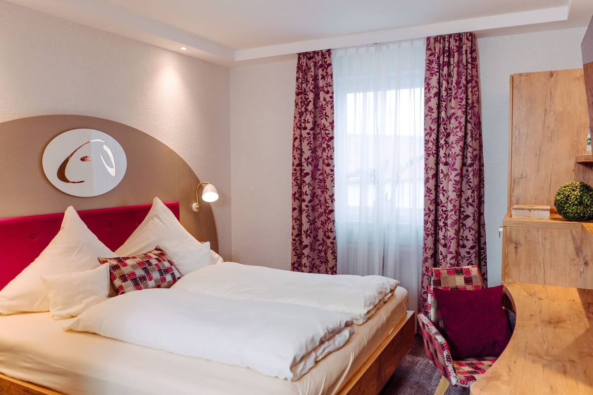 Quarto de hotel com cama, cabeceira, mesa de cabeceira, uma cadeira e um armário de madeira.