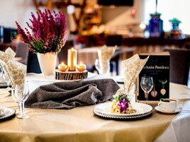 Mesa posta para refeição, com cardápio, velas e uma planta decorativa.