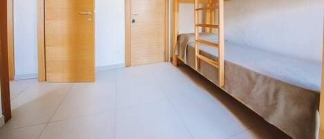Quarto com beliche, porta de madeira e piso ladrilhado.