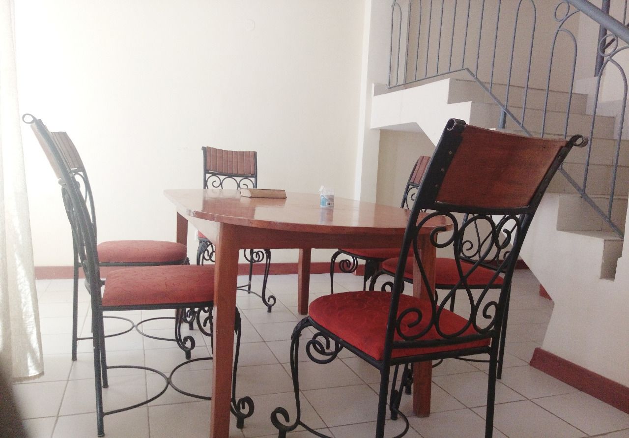 Uma sala de jantar com uma mesa de madeira e quatro cadeiras com almofadas vermelhas.