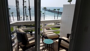 Uma varanda com vista para o oceano, palmeiras e um cais. Há cadeiras de vime e uma pequena mesa redonda.