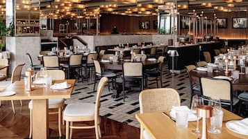 Restaurante com várias mesas e cadeiras, área de bar e escadaria que leva a um andar superior.