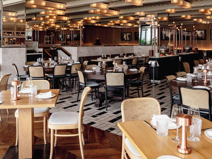 Restaurante com várias mesas e cadeiras, área de bar e escadaria que leva a um andar superior.