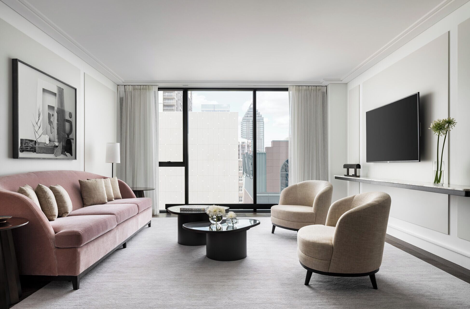 Uma sala de estar moderna com um sofá rosa, poltronas bege, uma mesa de centro e uma grande janela com vista para a cidade.