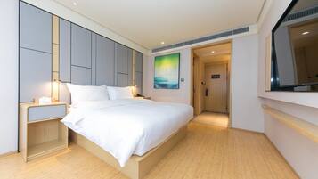 Quarto de hotel moderno com uma cama grande, mesas de cabeceira, um quadro e vista para o corredor.