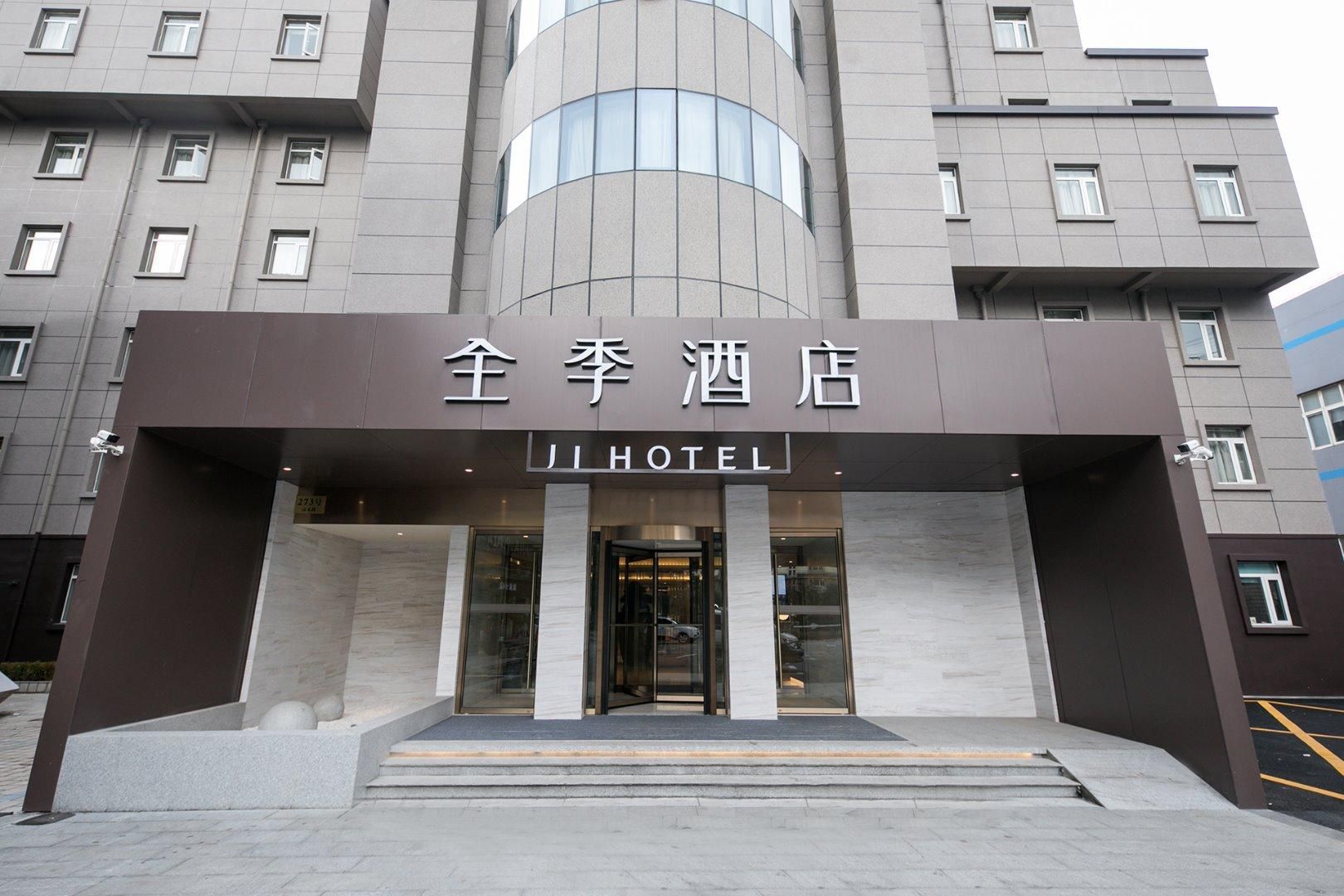 Entrada de hotel com fachada moderna, janelas amplas e uma placa com a inscrição 'JI HOTEL'.