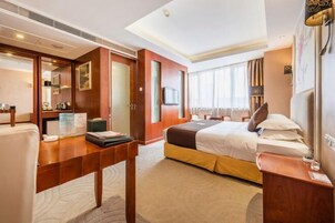 Quarto de hotel com cama, escrivaninha, cadeira, televisão e guarda-roupa.