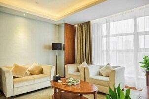 Quarto de hotel moderno com dois sofás, uma mesa de centro e uma janela grande com cortinas leves.