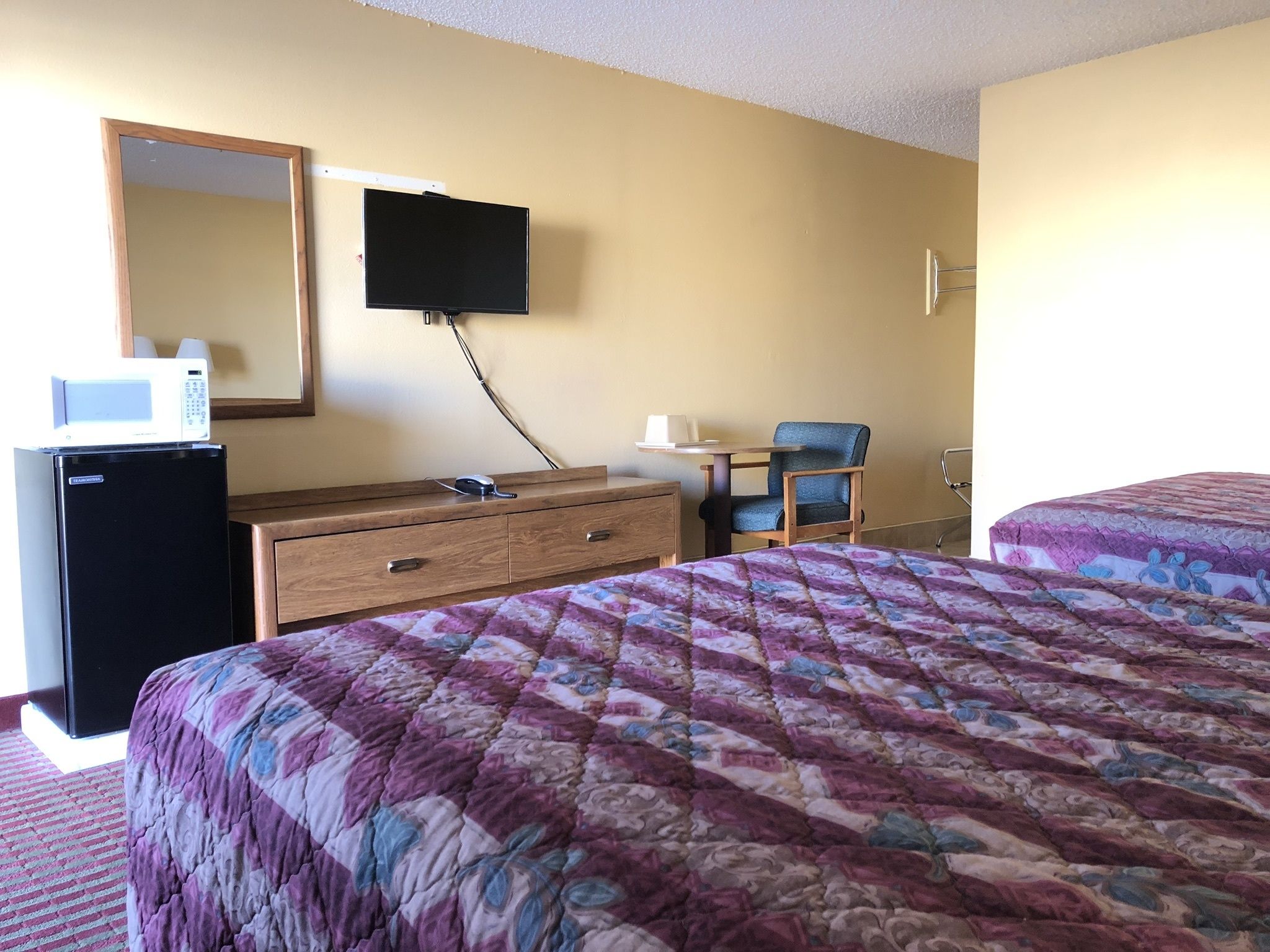 Quarto de hotel com duas camas, uma escrivaninha, uma cadeira, televisão e frigorífico.