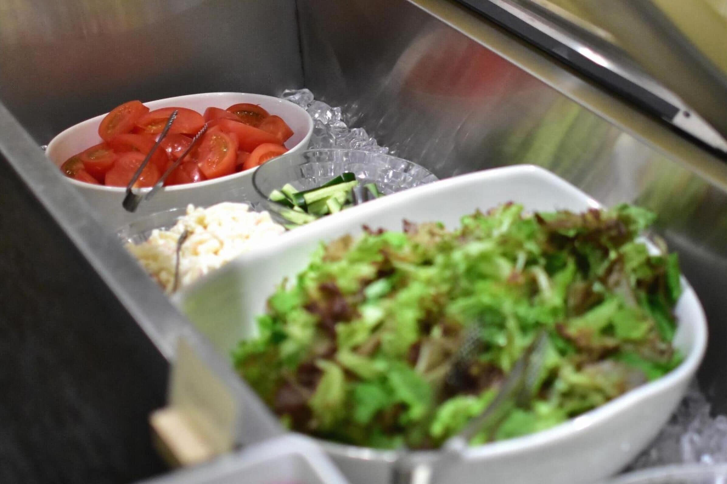 Buffet com diversos pratos, incluindo tomates fatiados, salada verde e arroz.