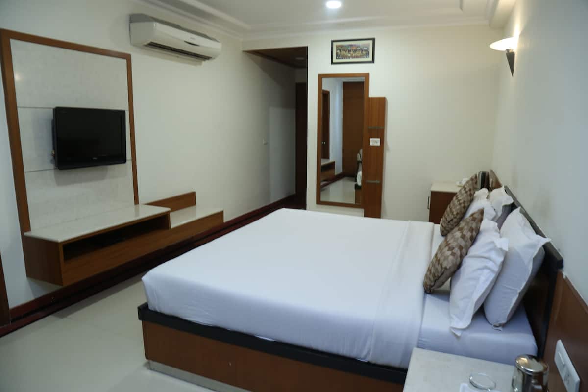 Quarto de hotel com cama, televisão na parede, mesa de cabeceira e espelho.