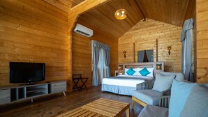 Interior de uma cabana de madeira com cama, sofá, televisão e mobiliário de madeira.