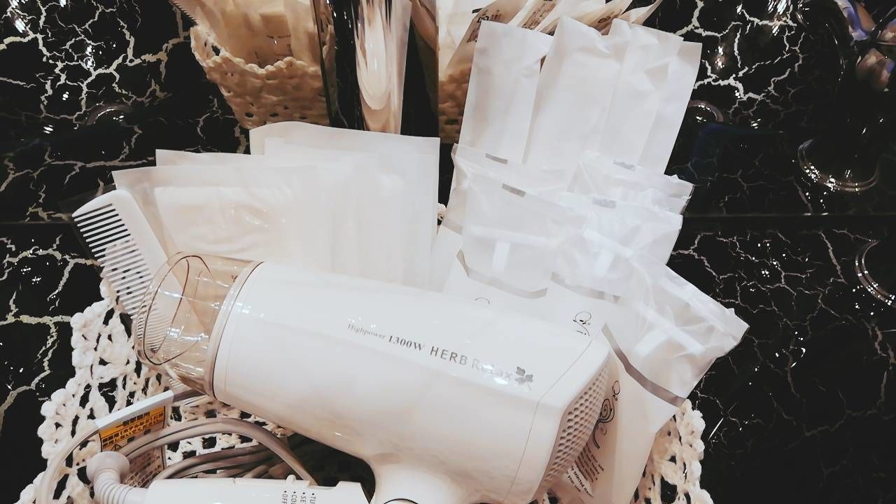 Um secador de cabelo branco com uma etiqueta, rodeado por sacos de papel brancos sobre uma superfície de mármore preto.