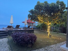 Uma área de estar à beira-mar com espreguiçadeiras e guarda-sóis, um gazebo e uma árvore decorada com luzes.