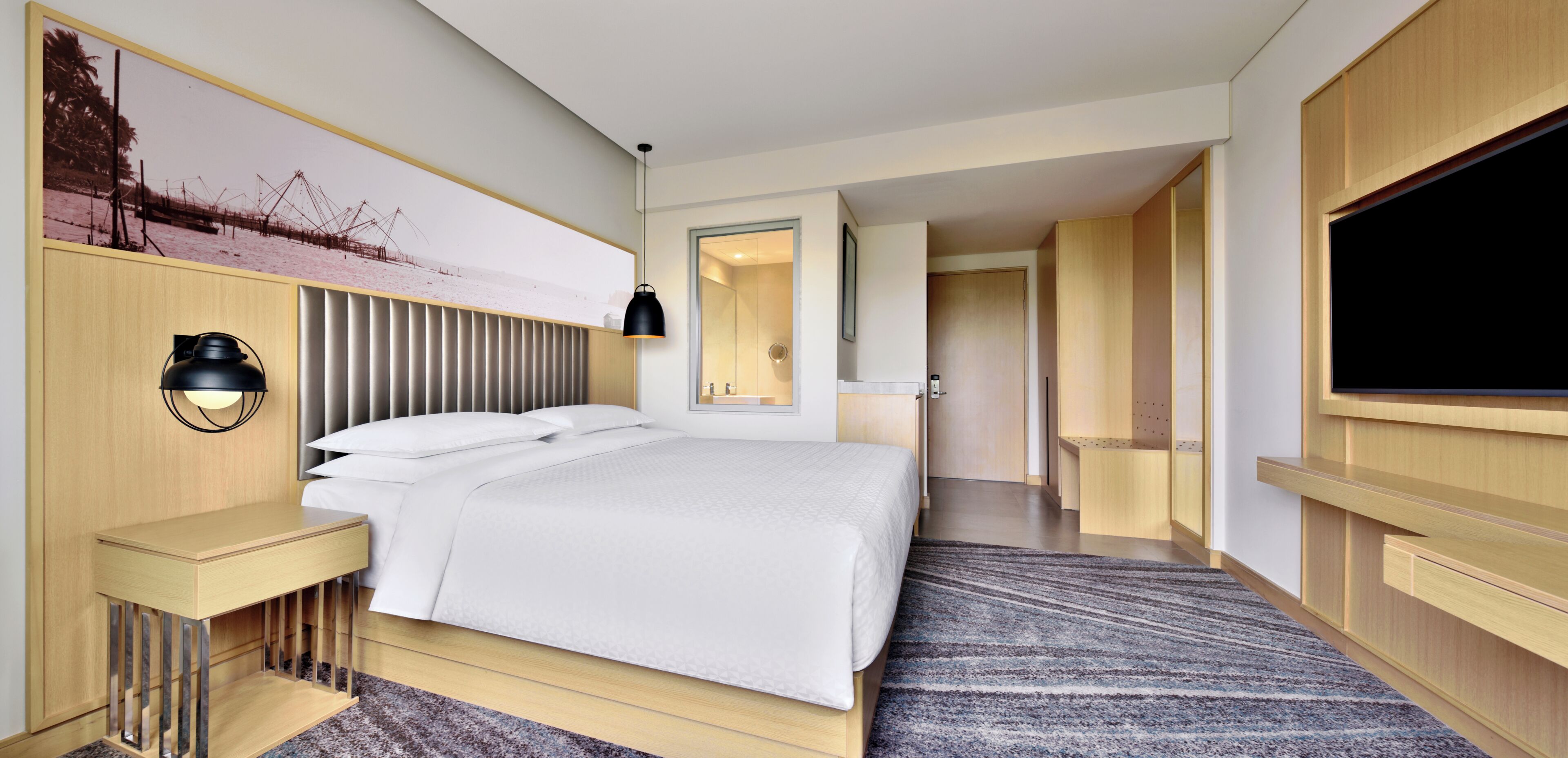 Quarto de hotel moderno com uma cama grande, uma escrivaninha, uma televisão e uma obra de arte na parede.