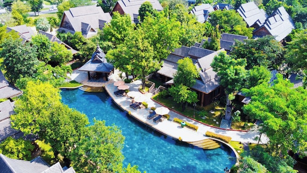 Vista aérea de um resort com uma piscina central, diversas villas para hóspedes e vegetação exuberante.