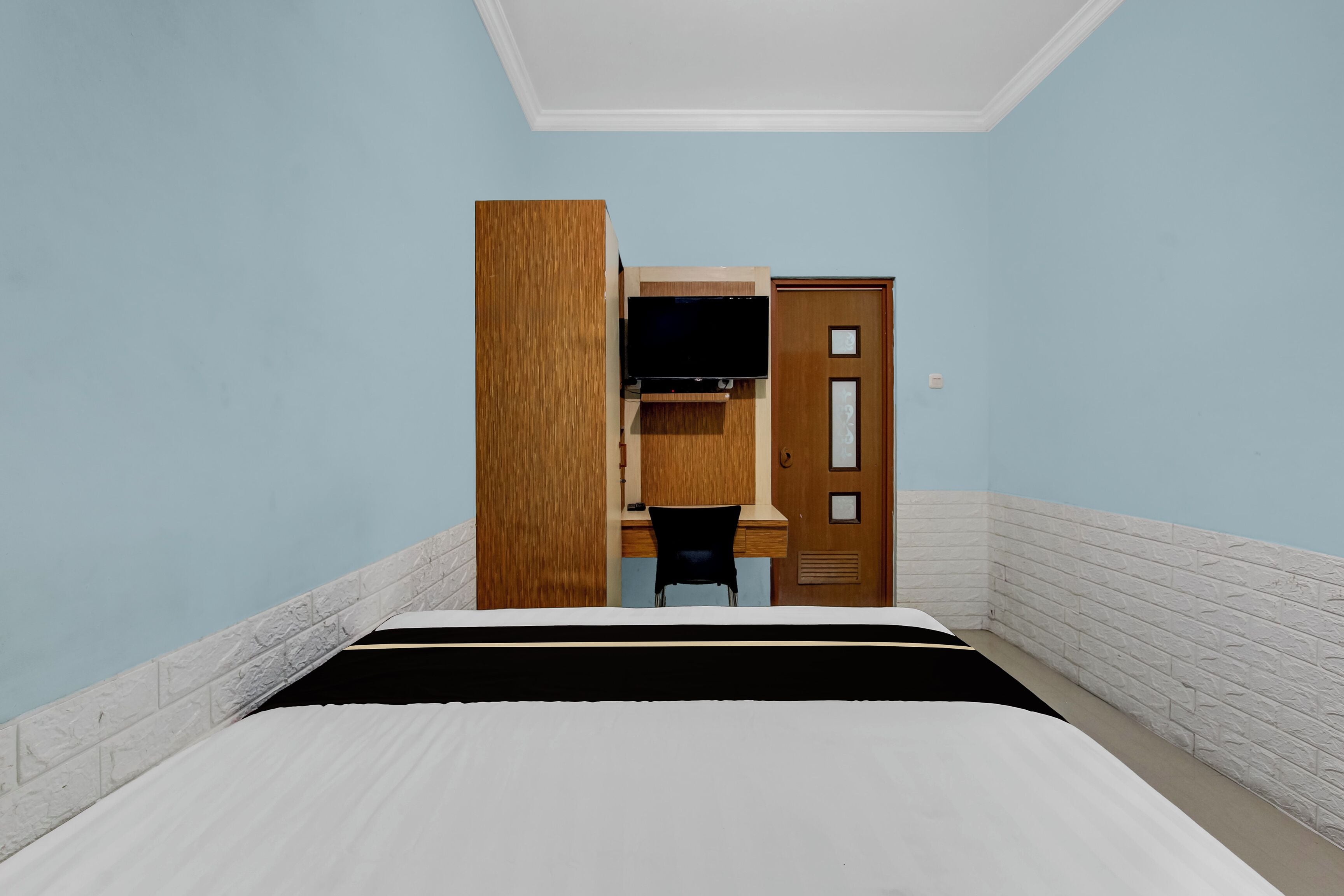 Um quarto com uma cama, uma escrivaninha com cadeira, uma televisão e uma porta.