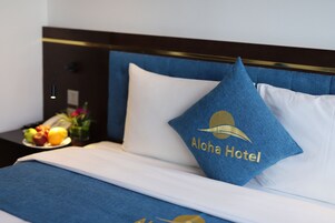 Uma cama de hotel com um travesseiro azul exibindo o logotipo e o nome do hotel, um travesseiro branco e uma colcha branca bem esticada.