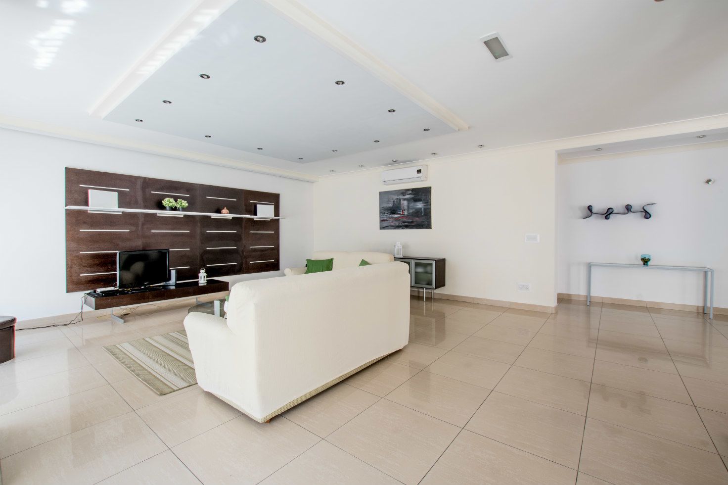 Uma sala de estar moderna com um sofá branco, uma televisão de tela plana, um móvel para entretenimento de madeira e uma pequena mesa lateral.