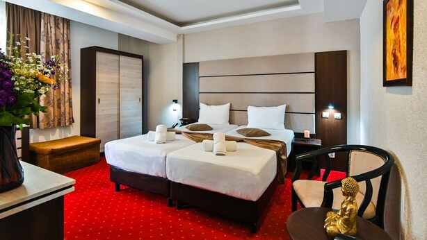 Quarto de hotel com duas camas, uma escrivaninha, uma cadeira, um tapete vermelho e um quadro na parede.