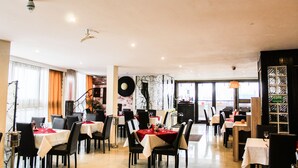 Um restaurante com mesas postas para refeições, uma grande parede decorativa e vista pelas janelas.
