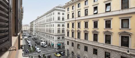 Vista da rua de uma cidade com edifícios históricos, um cruzamento movimentado e veículos estacionados.