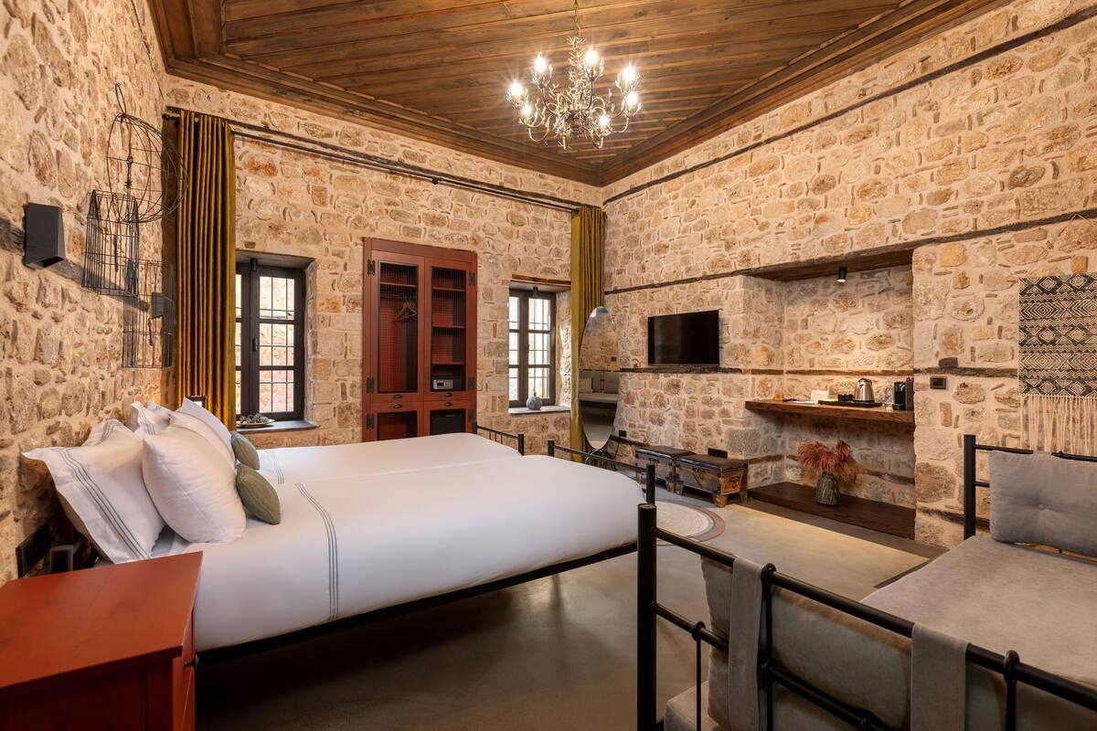 Quarto com parede de pedra, cama, televisão e teto de madeira.