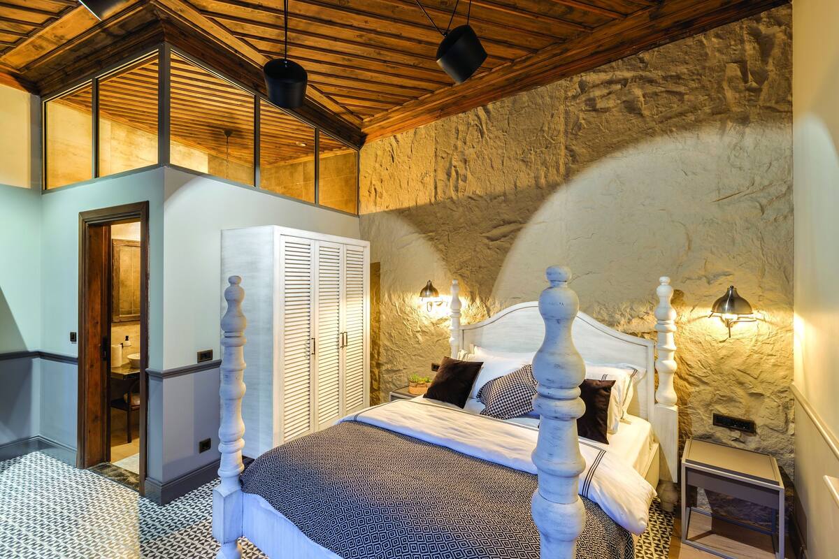 Quarto com cama de dossel, parede de pedra e teto de madeira.